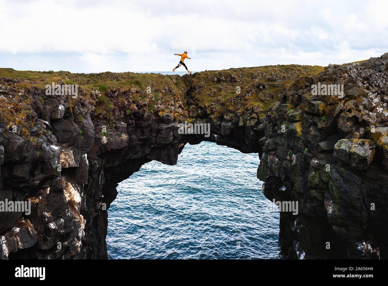 Tourist jumps over a natural rock bridge in Arnarstapi, Iceland Stock ...