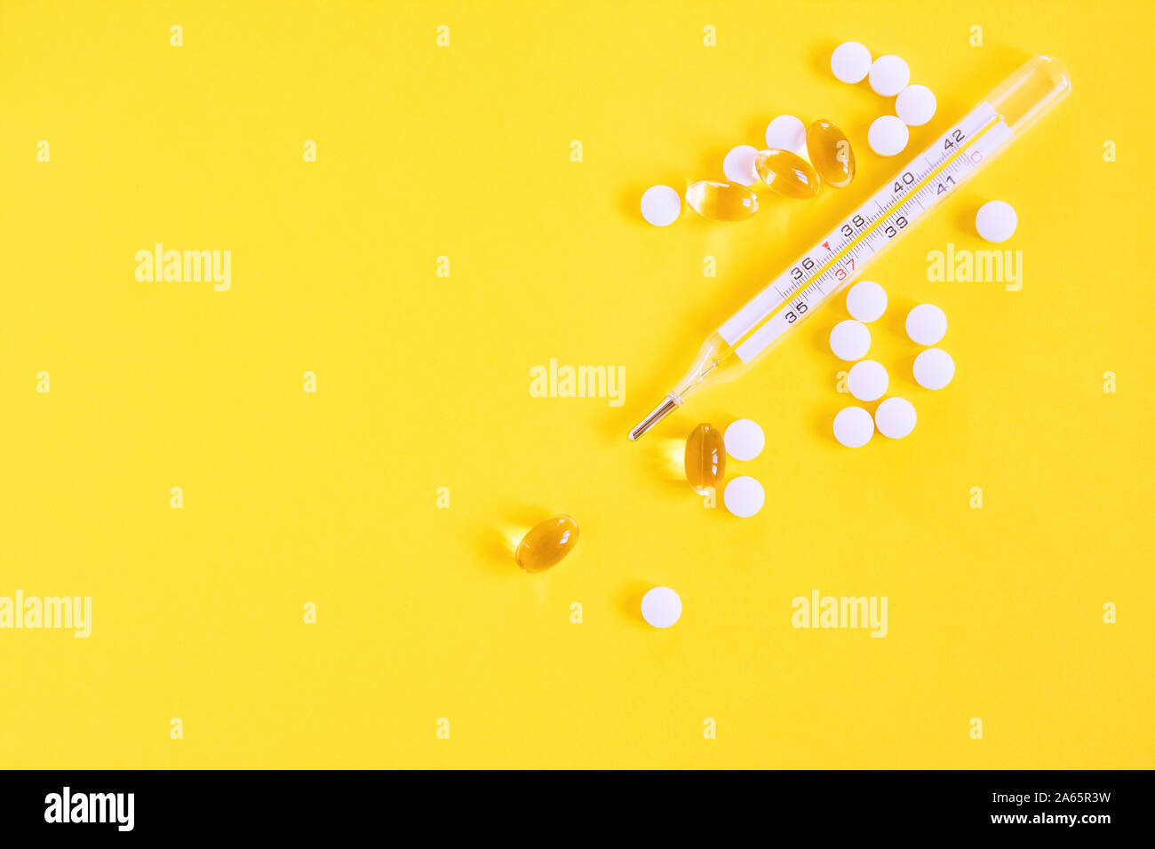 Glass mercury thermometer, white pills and capsules on yellowbackground ...