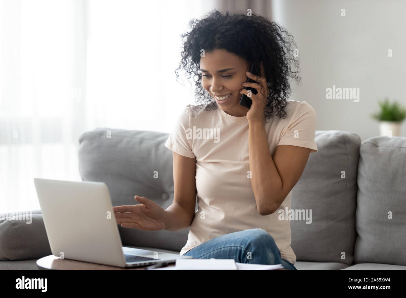 Smiling black woman multitask at home using gadgets Stock Photo - Alamy