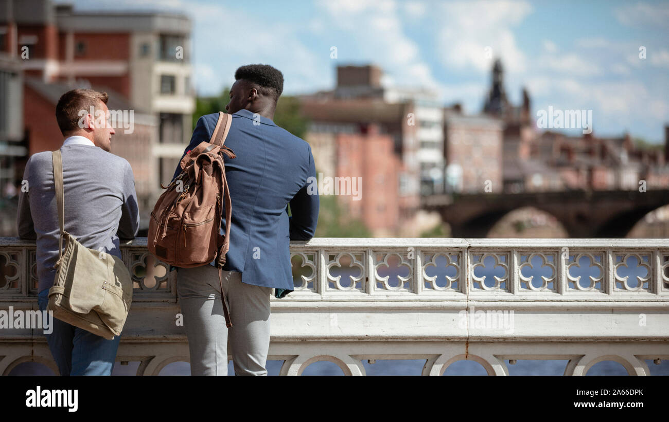Two businessmen talking while leaning on a bridge in York.They have ...