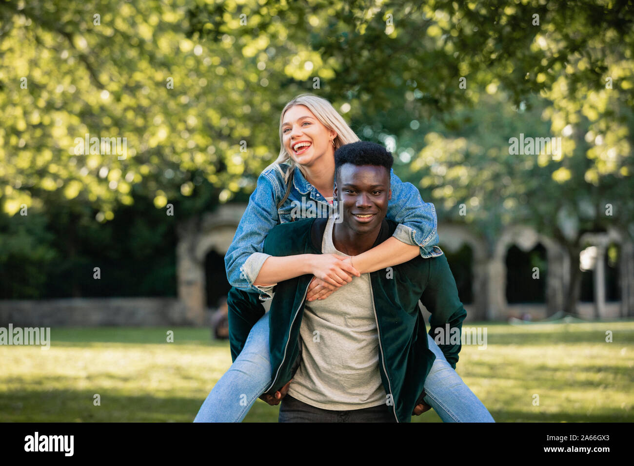 A man giving a woman a piggyback lift through a park. They are both ...