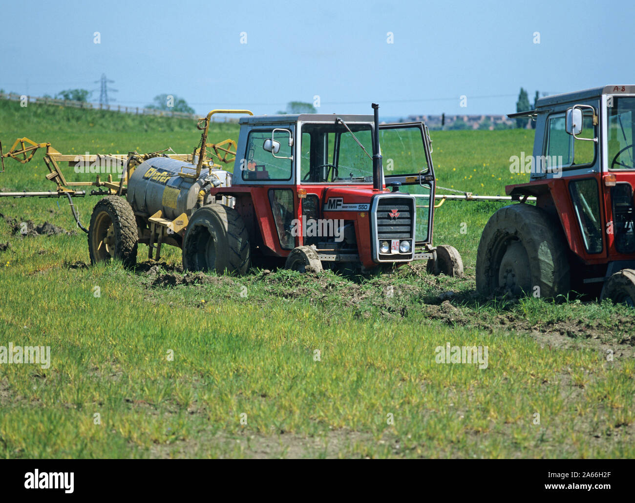 Two tractors, one with a sprayer, the other rescuing, bogged down in a ...