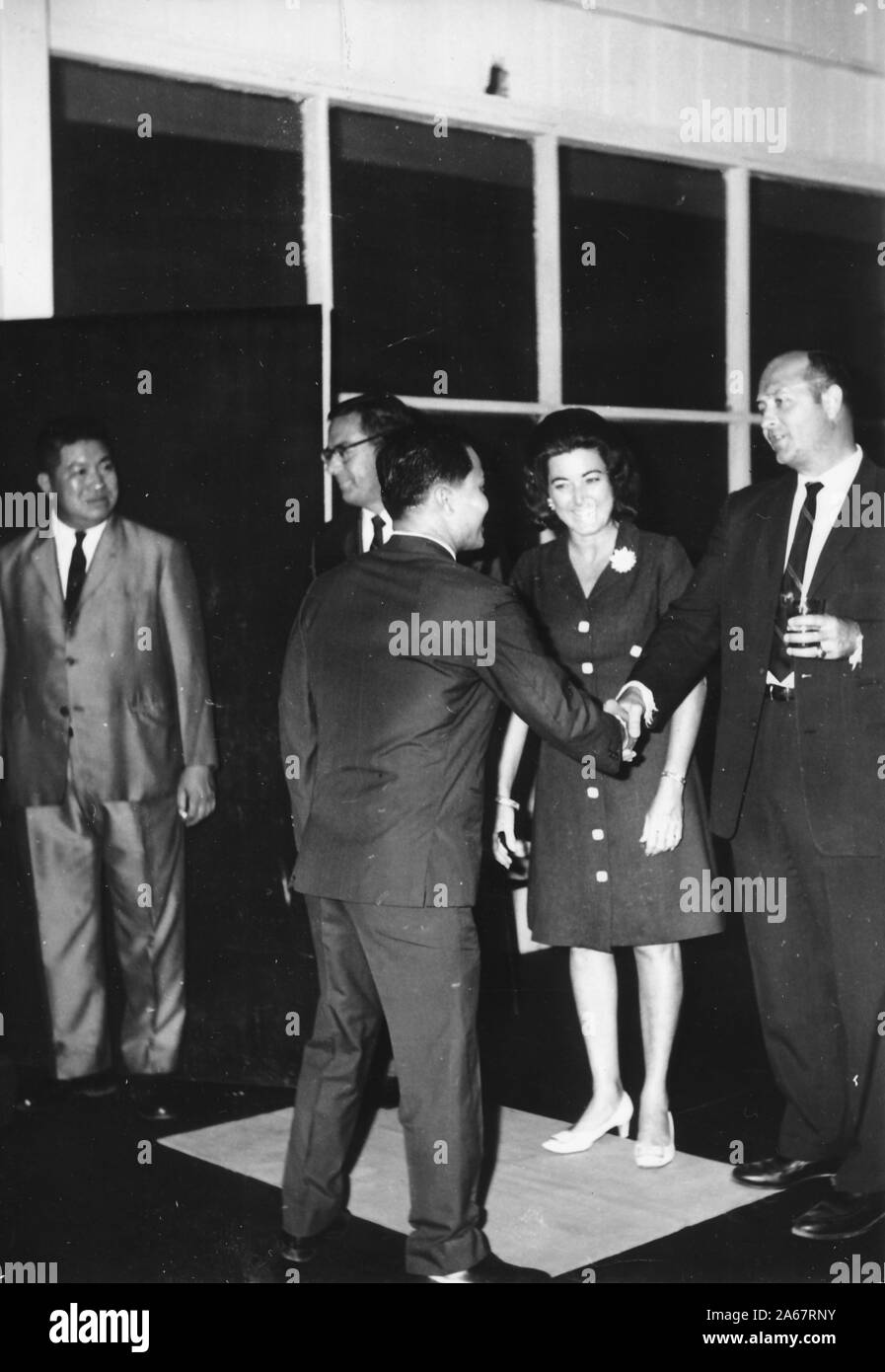 A group of formally dressed men and women greet each other in a ...