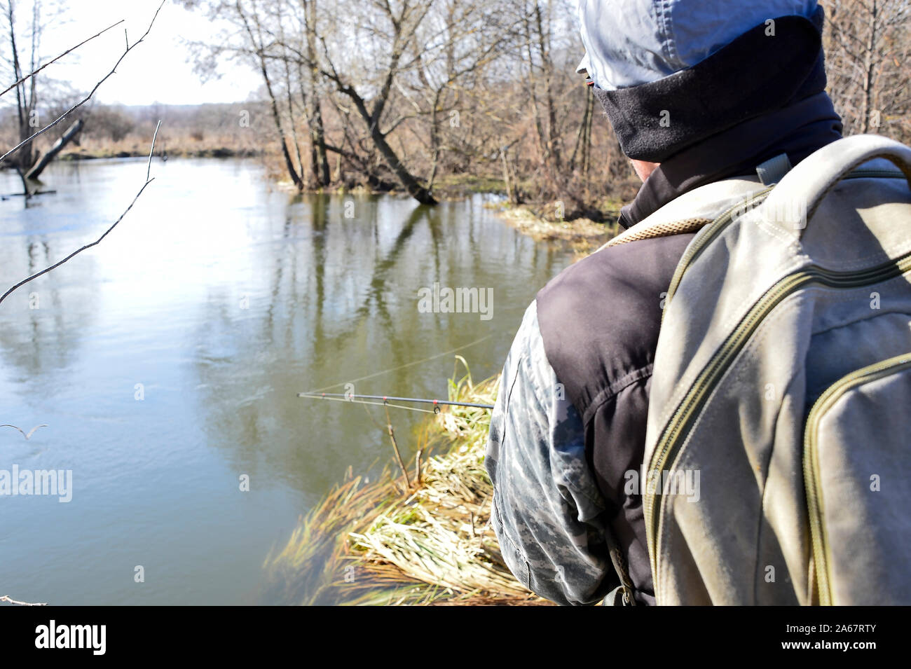 A male angler catches a predator spinning in a cold river. Rear view ...