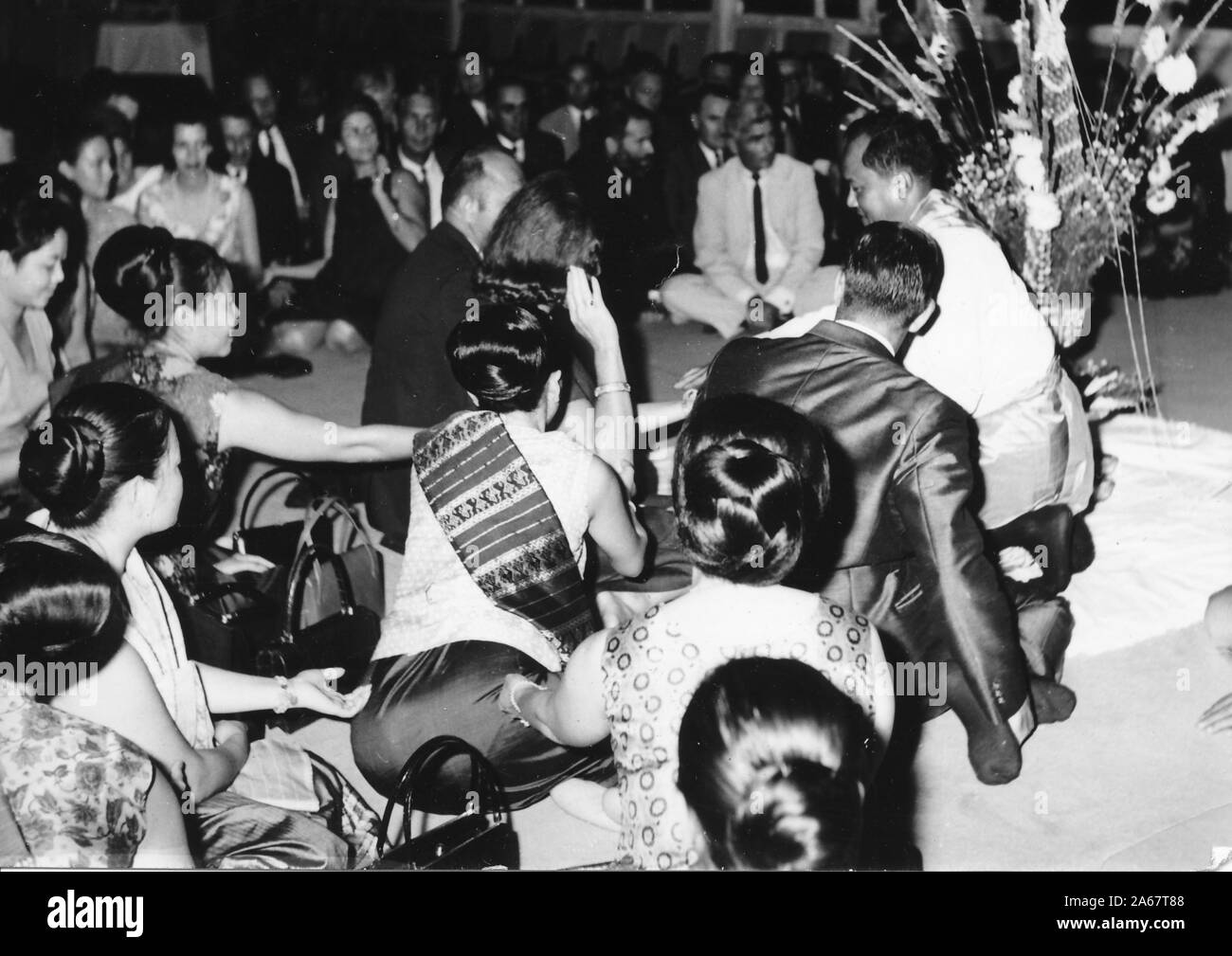 A group of formally dressed men and women sit on the floor, some ...