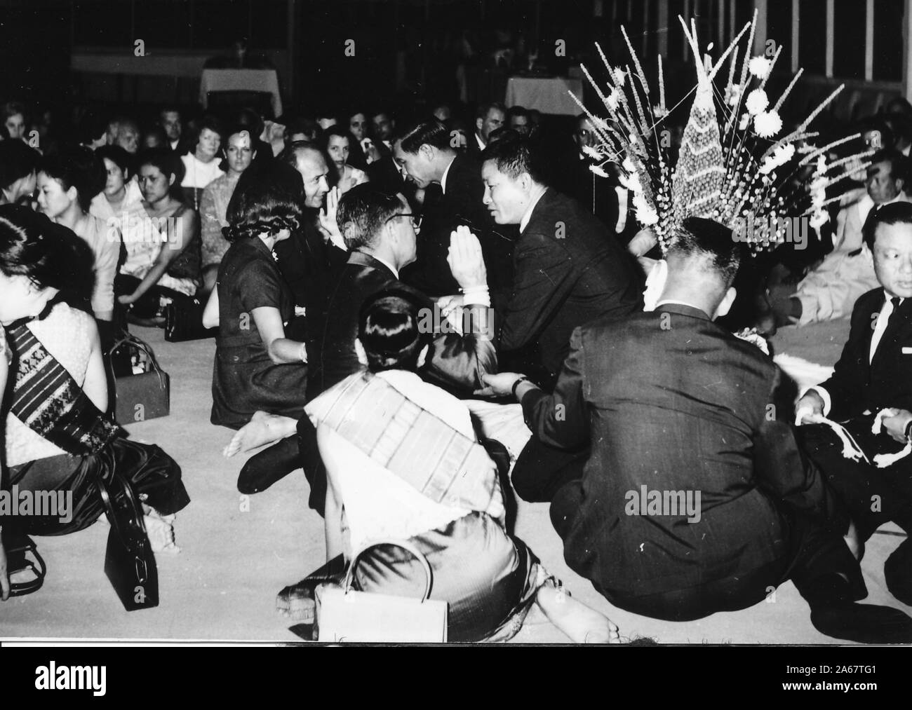 A group of formally dressed men and women sit on the floor, tying and ...