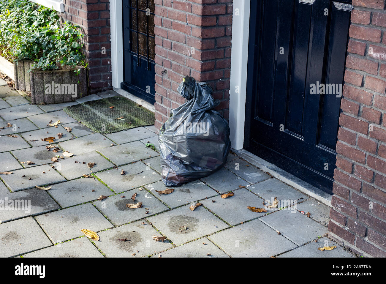 Garbage bag near a front door in a neighbourhood, ready for pick up ...