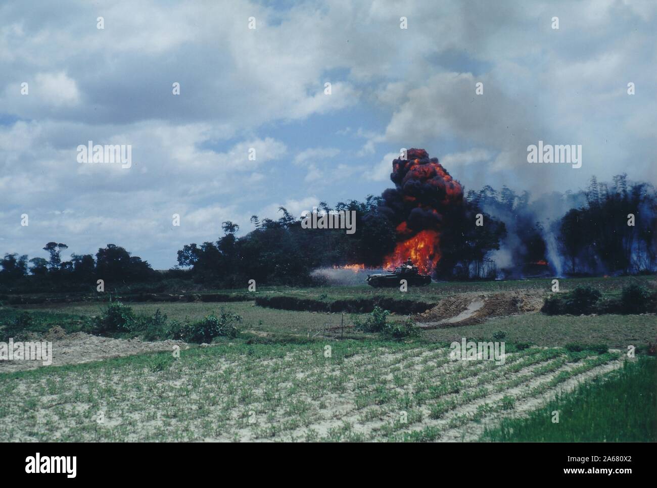 Wide shot, across an open field, of a military vehicle passing a ...