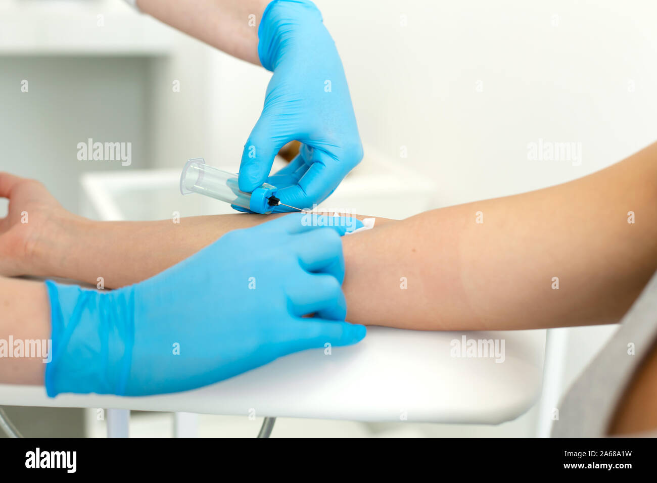 a gloved nurse inserts a needle into a vein on the patients arm and ...