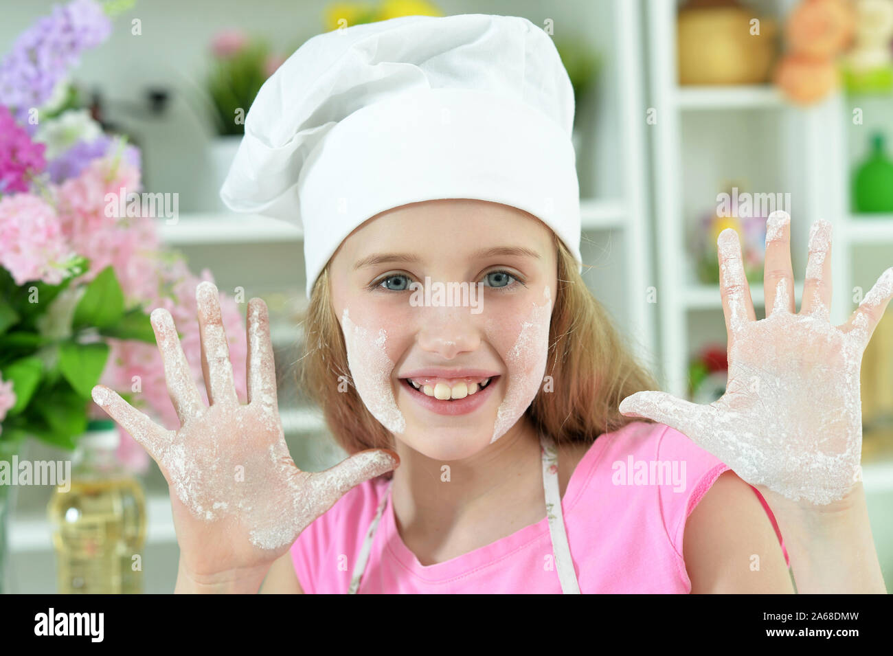 Cute girl in chefs hat showing palms covered with flour Stock Photo - Alamy
