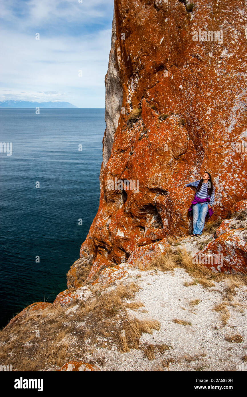 A girl stands under a high rock and enjoys with her eyes closed by the ...