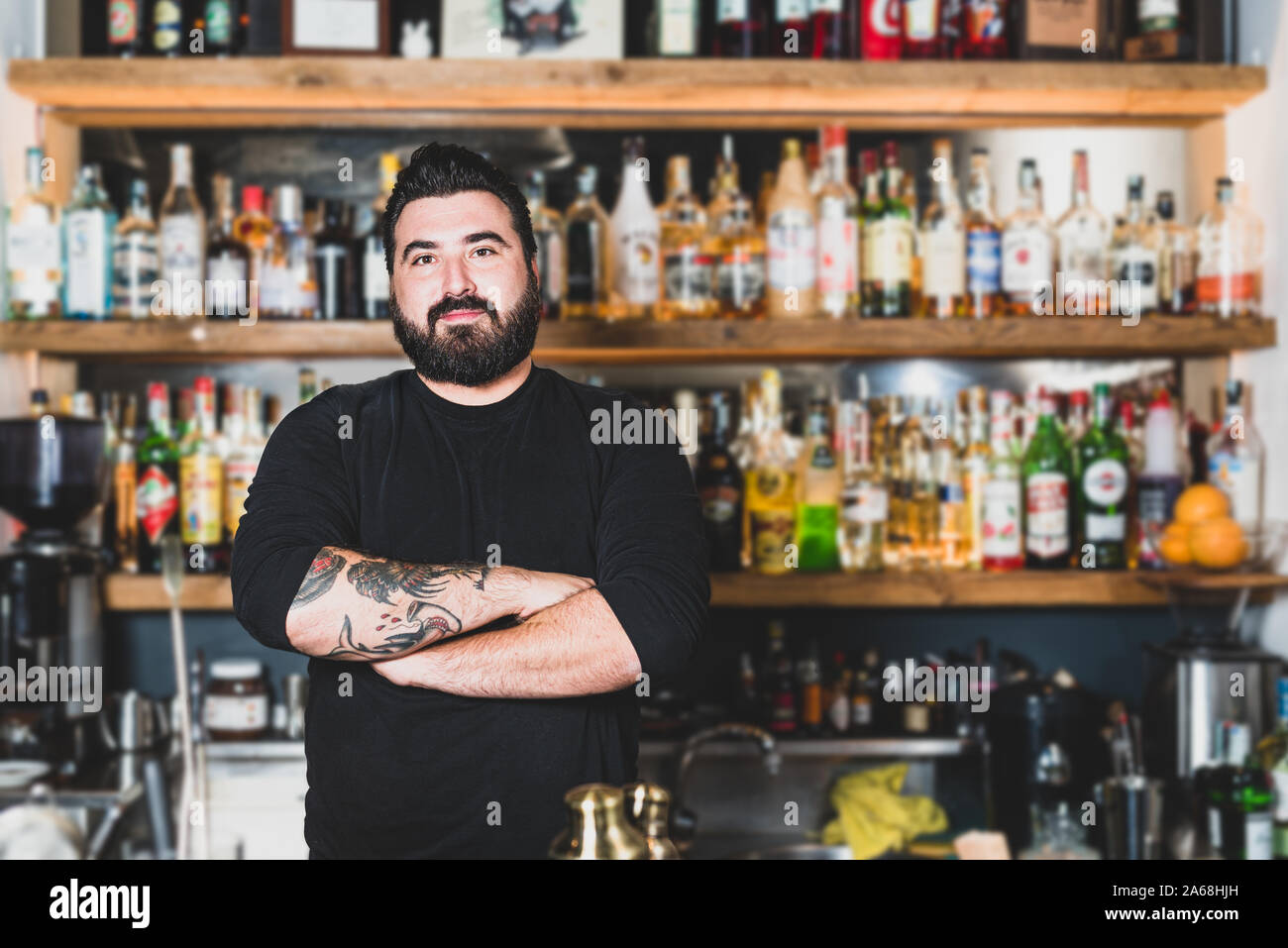 Young hipster bartender with thick beard smiles at the counter with a ...
