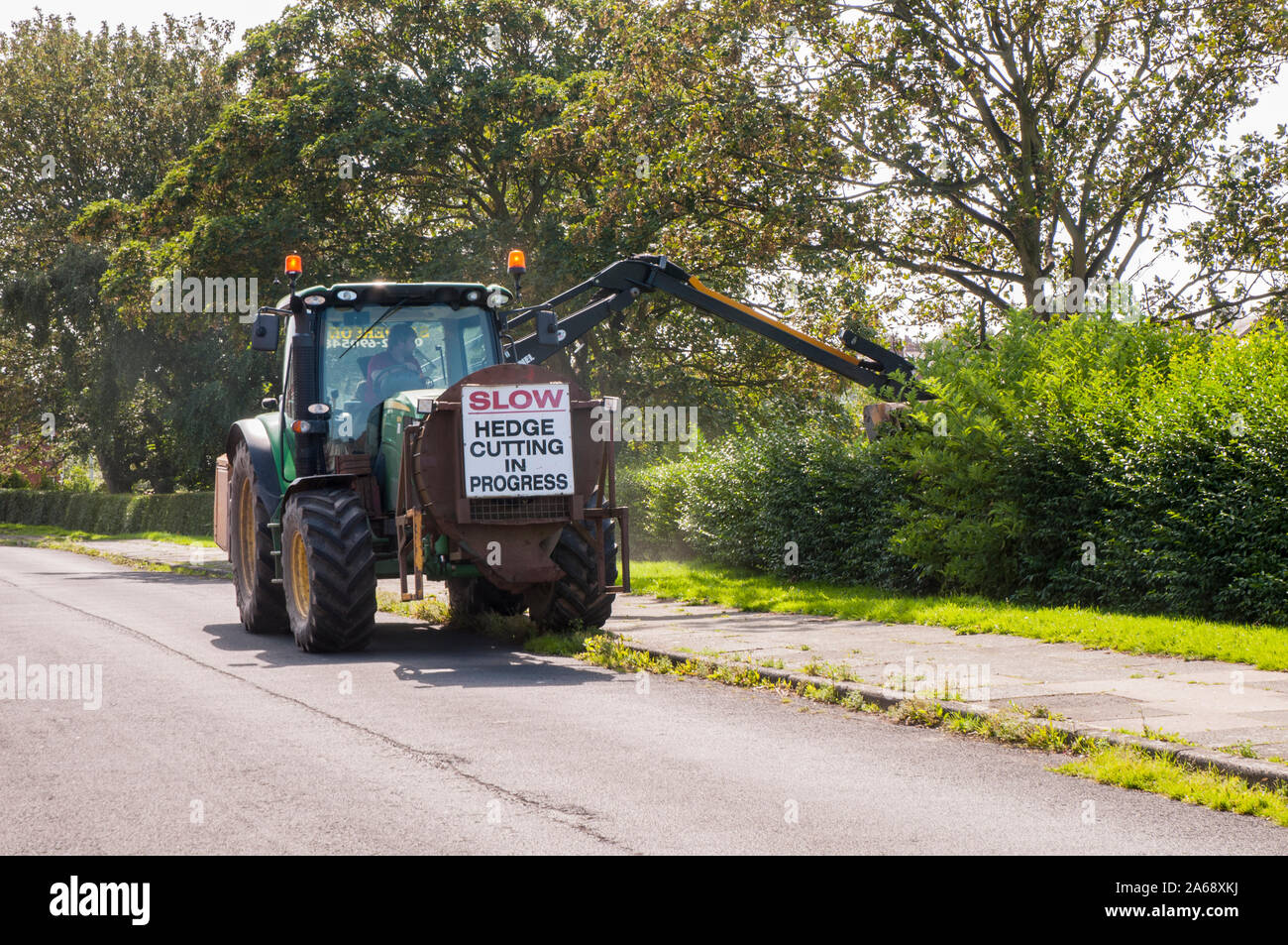 Tractor with extending cutter arm cutting hedge around local park ...