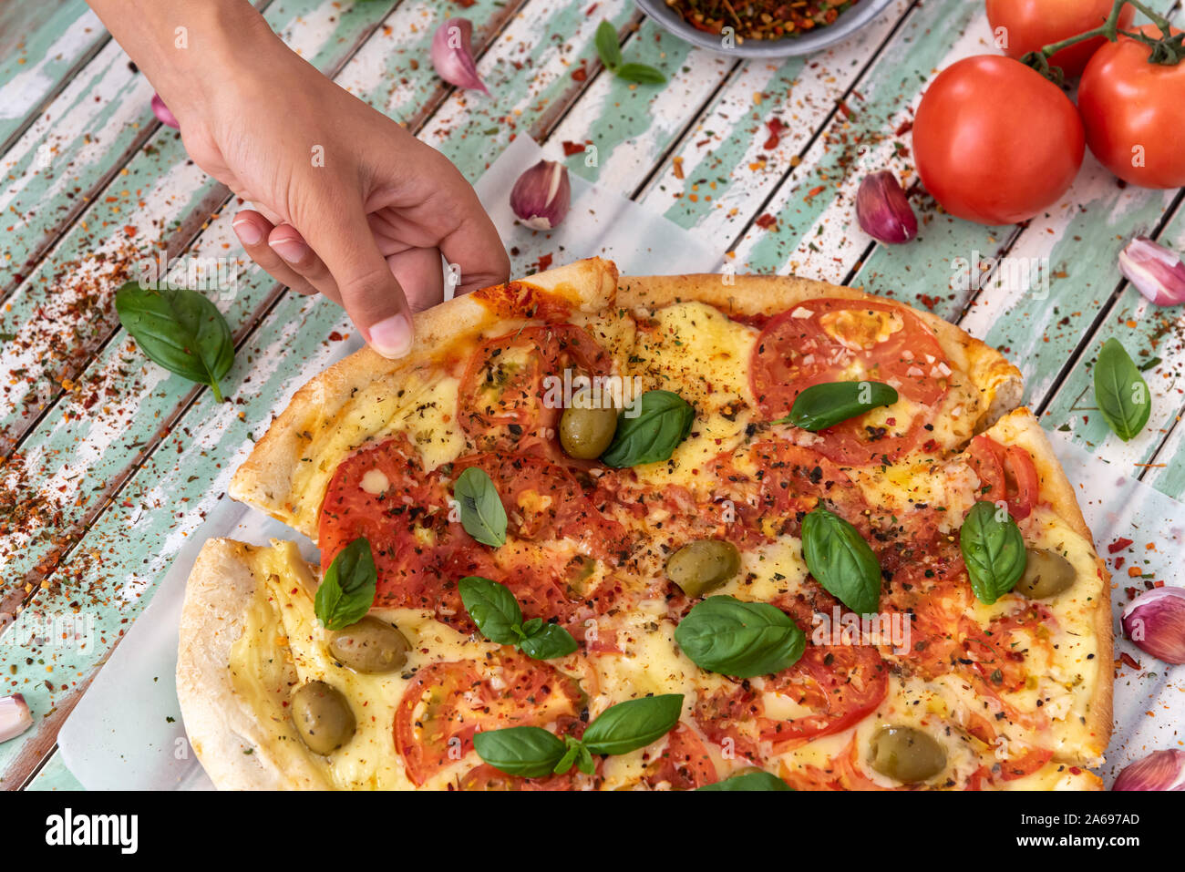 Hand of a woman taking a slice of a pizza viewed from above on rustic ...