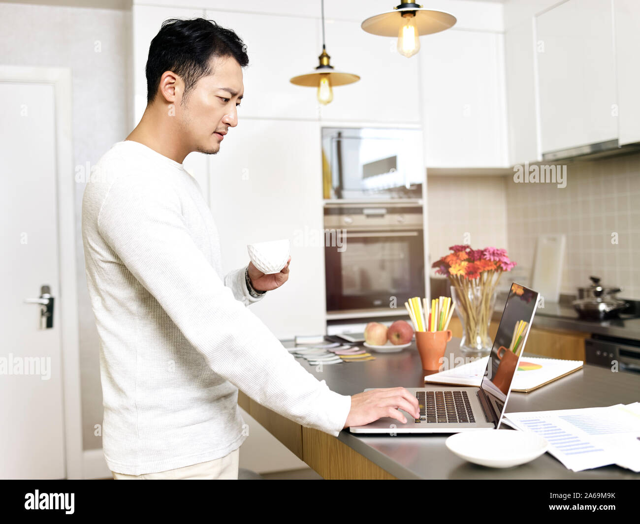 young asian man working from home standing by kitchen counter using ...