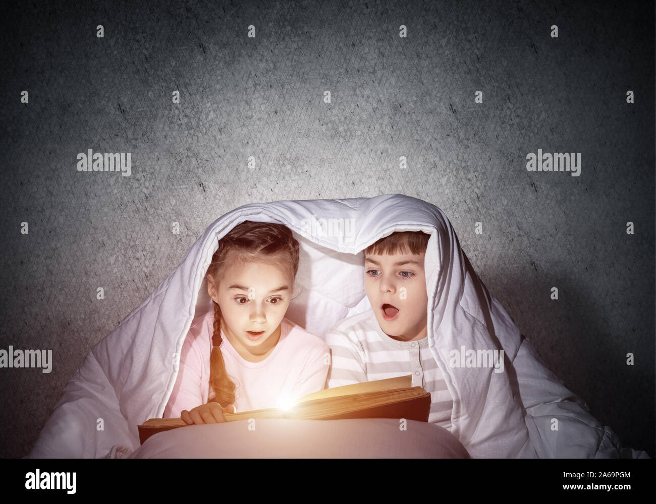 Surprised children reading scary stories in bed before going to sleep ...