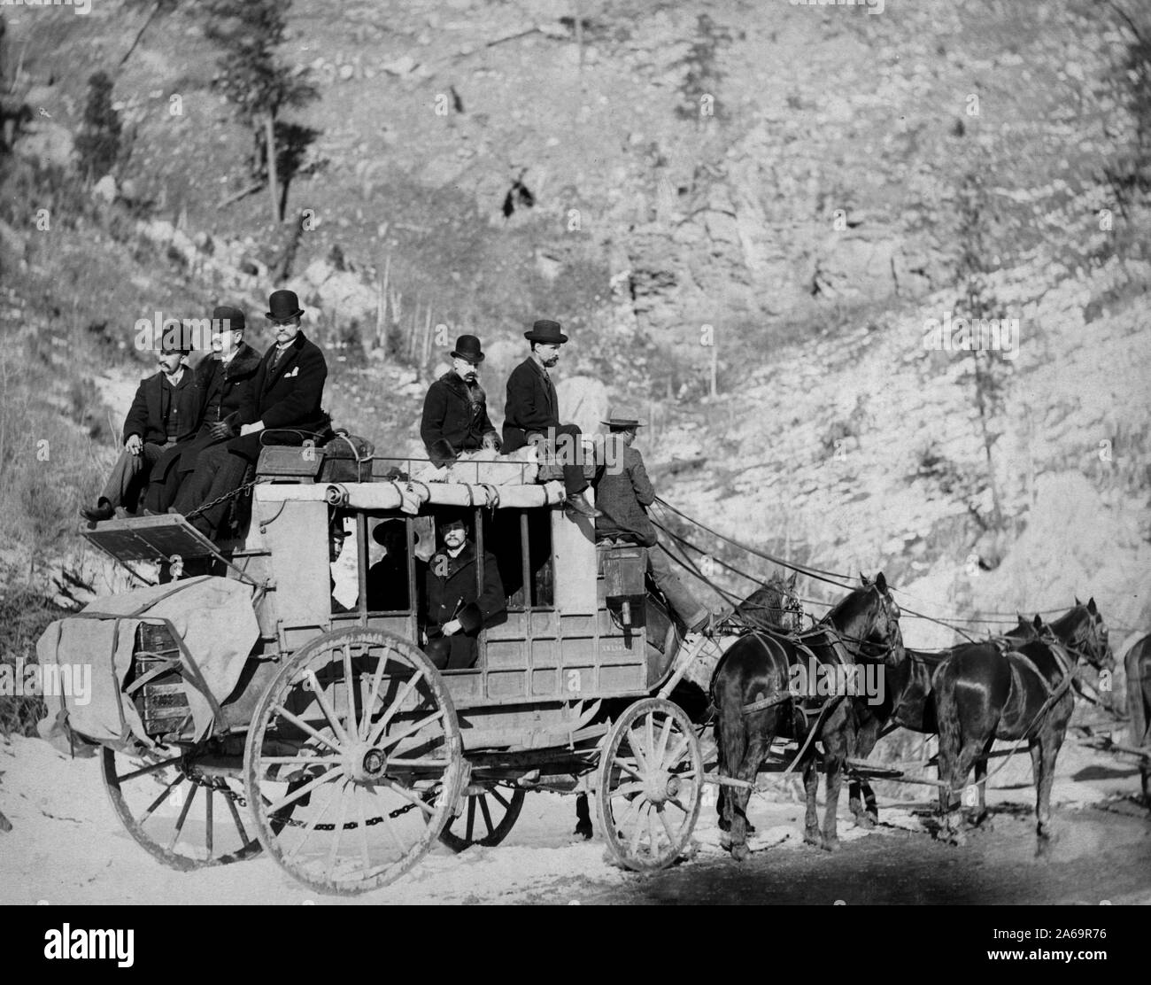 Side view of a stagecoach; formally dressed men sitting in and on top ...