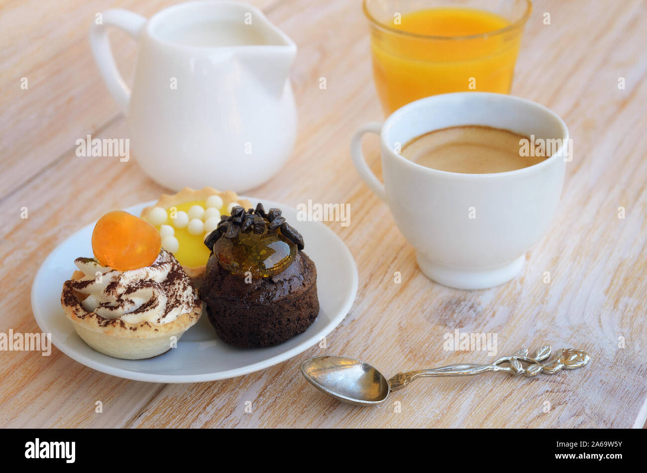 Cup of expresso coffee, milk jug,orange juice and cute mini cakes on ...