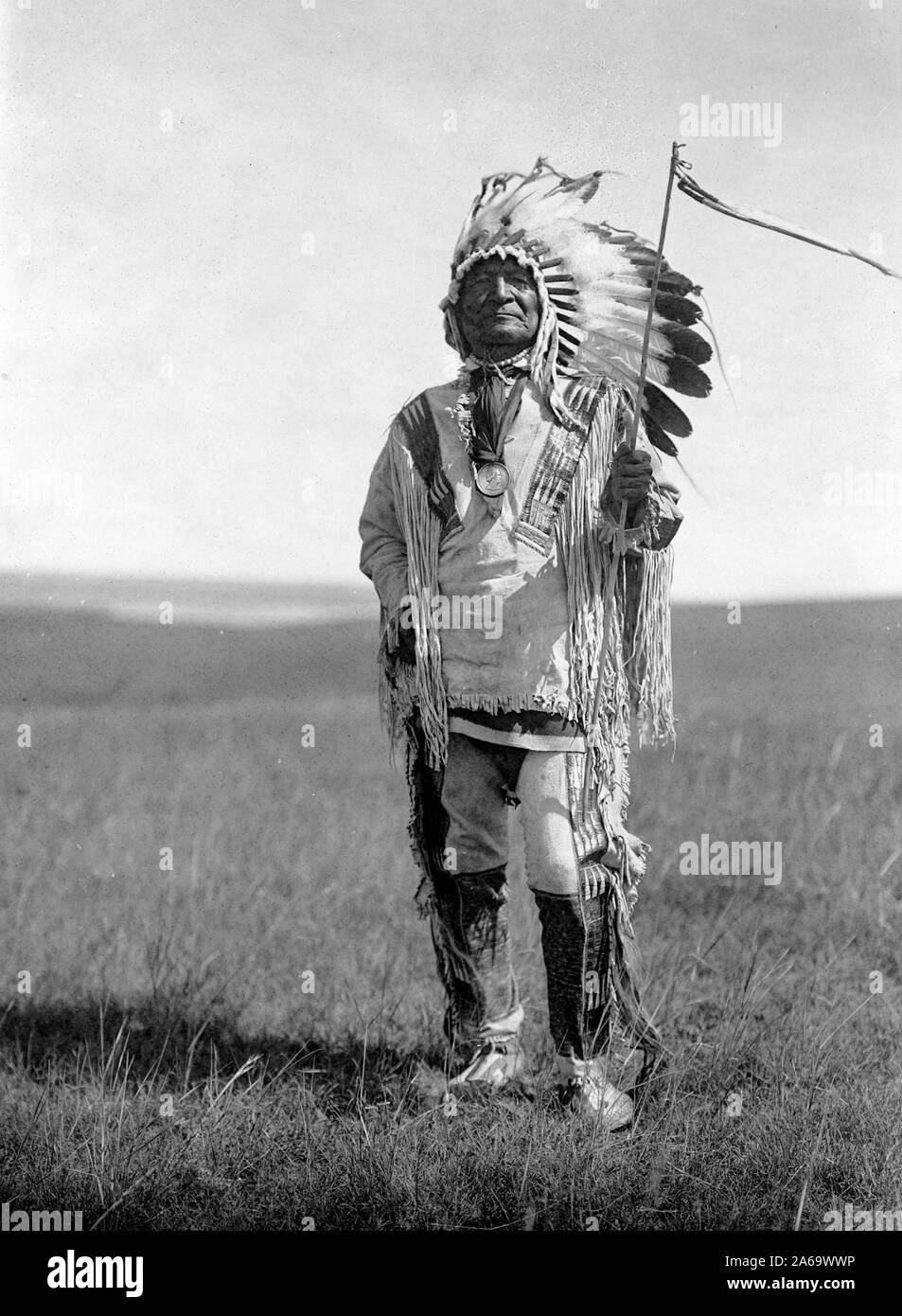 Photograph shows Sitting Bear, an Arikara chief, in full regalia, with ...