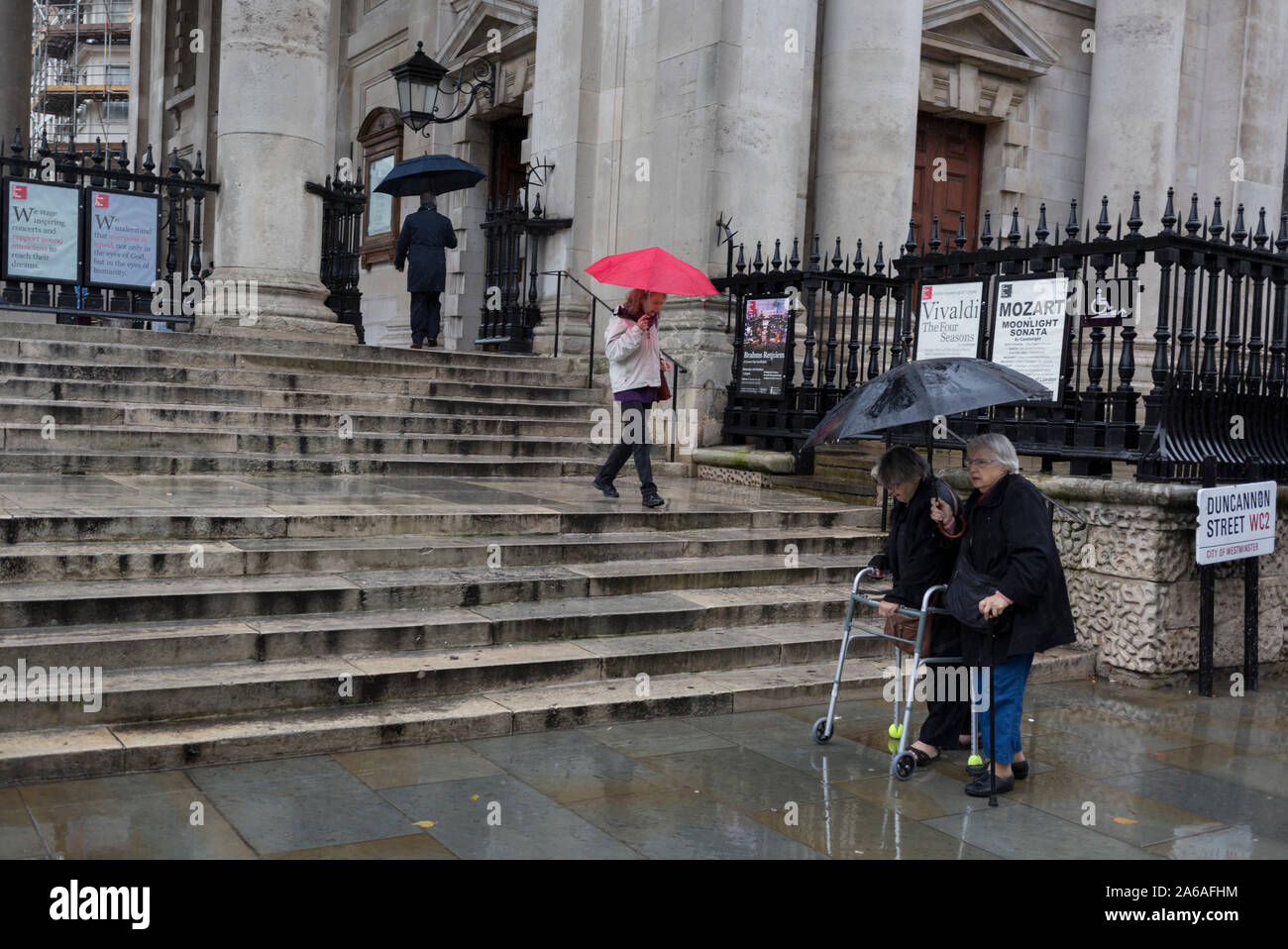 An elderly lady using a Zimmer frame endures heavy rainfall on an ...