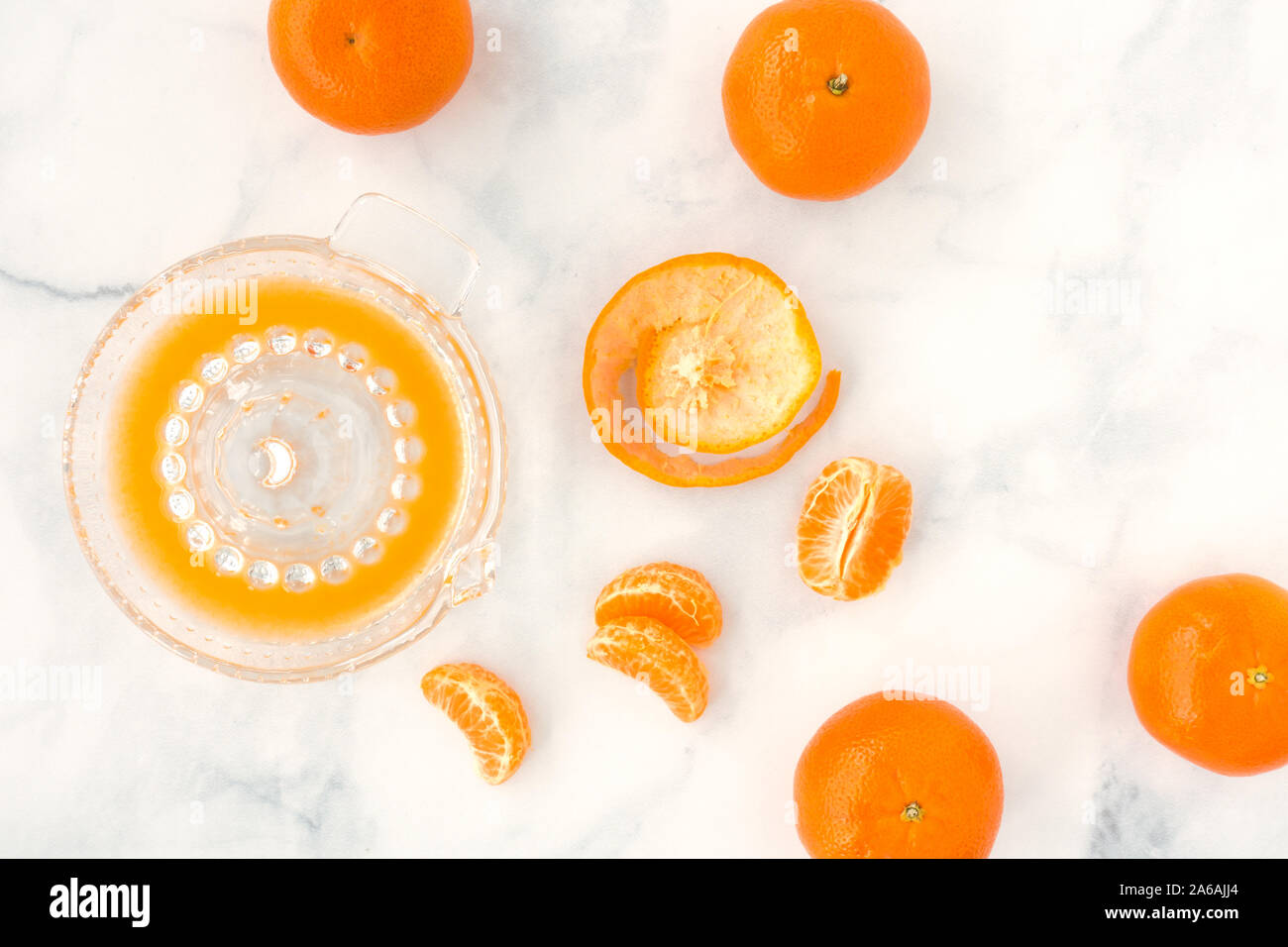 Citrus glass juicer with juice and clementines on white marble ...