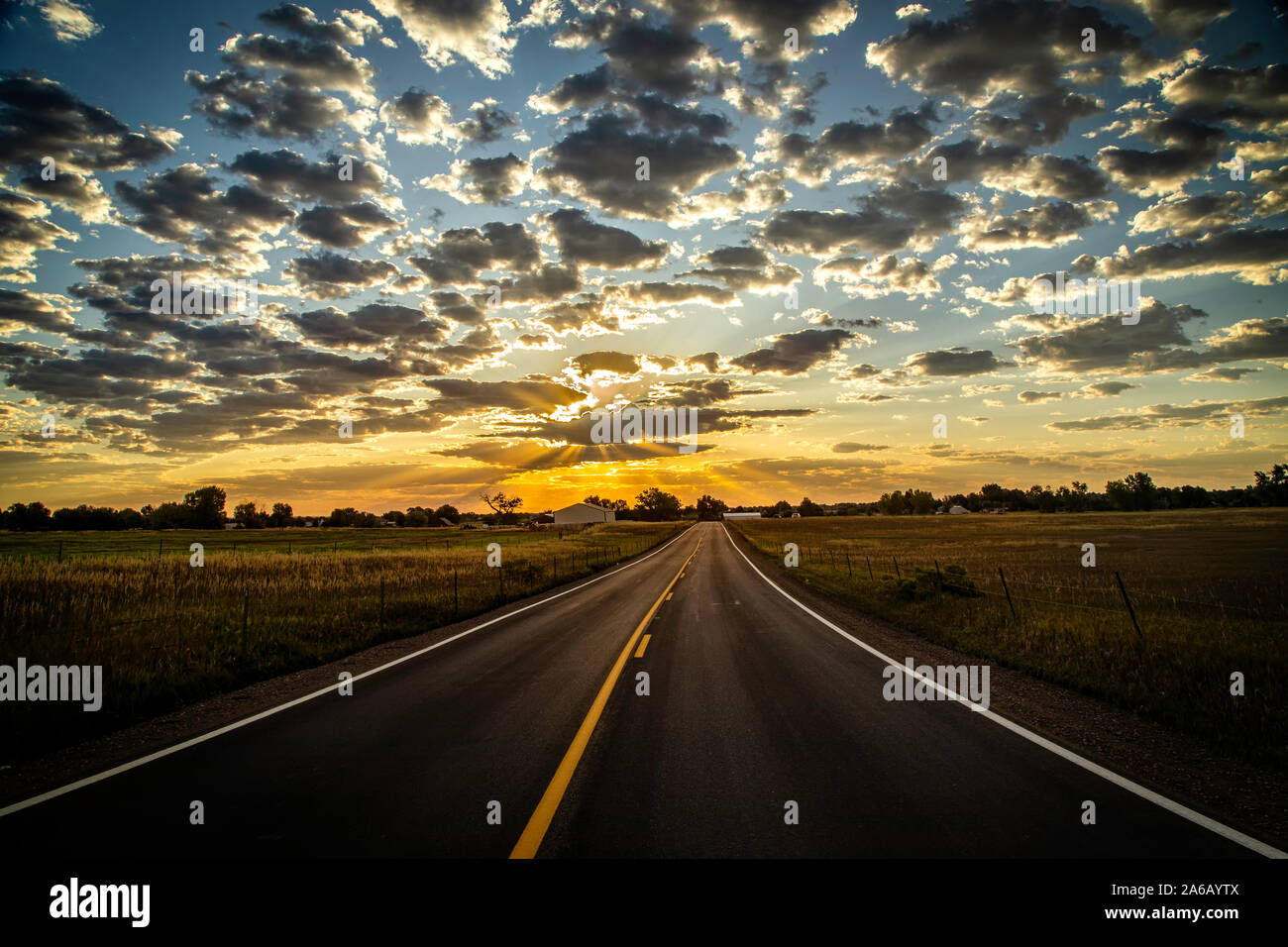 A country Paved Road leading into the Horizon as sun rays beam out of ...