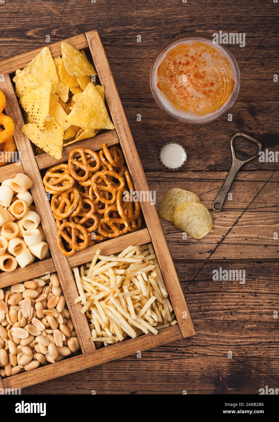 Glass of craft lager beer and opener with box of snacks on wood ...