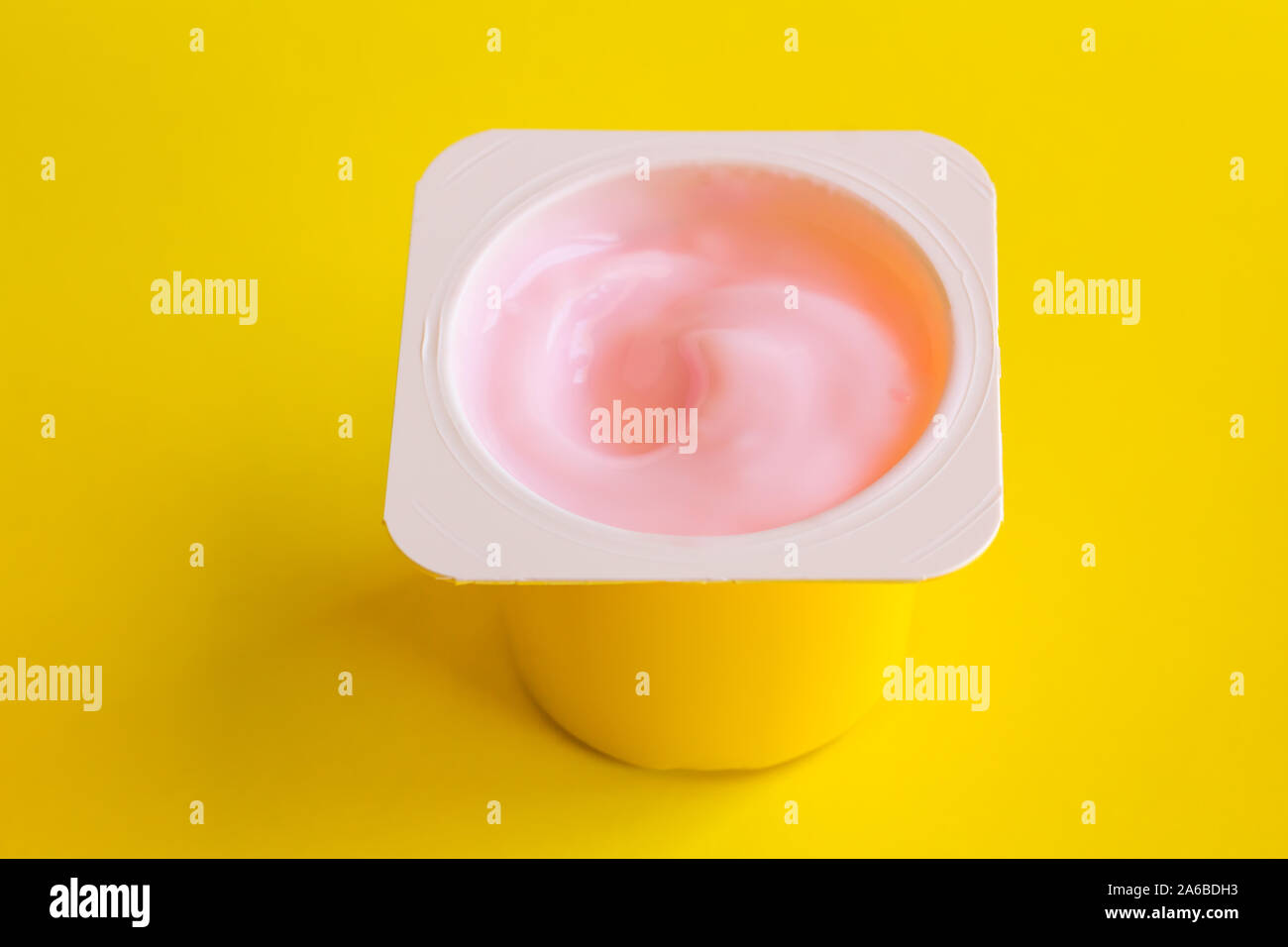 Strawberrry pink yogurt in yellow plastic cup isolated on bright yellow ...
