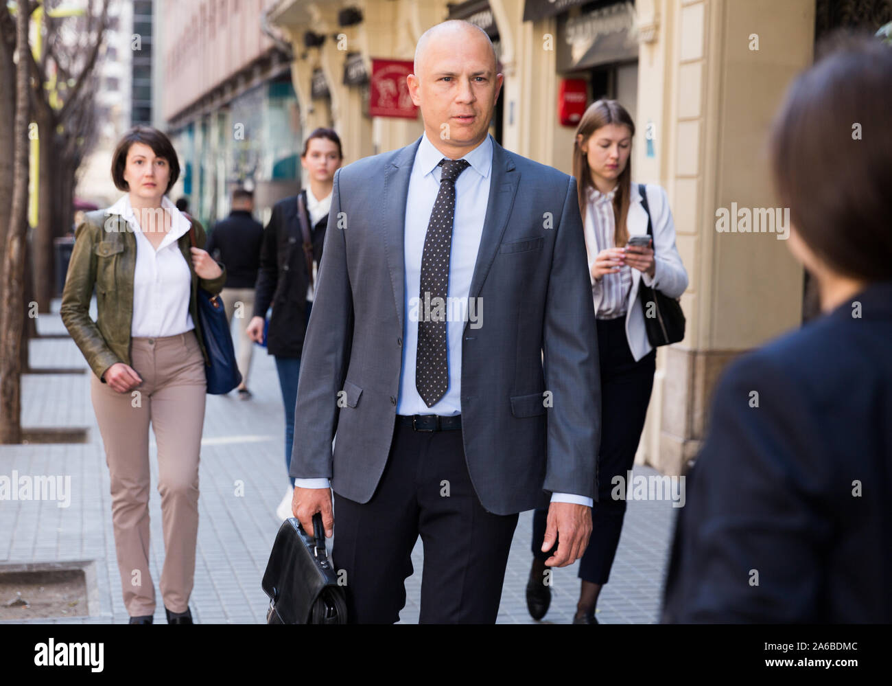 Focused business man with briefcase in hand walking on city street in ...