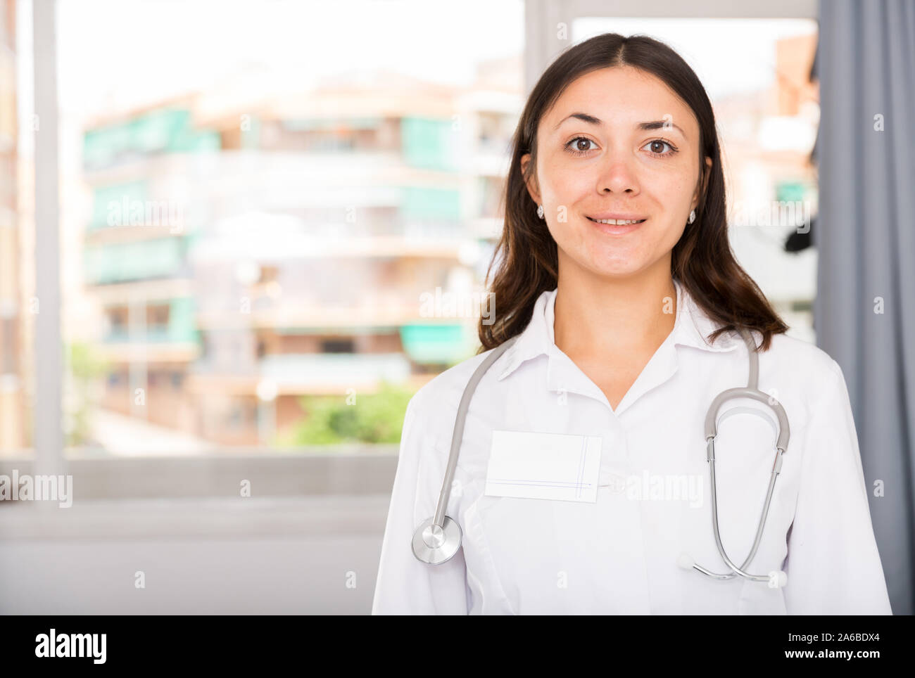 Portrait of young female practitioner in white uniform standing in ...
