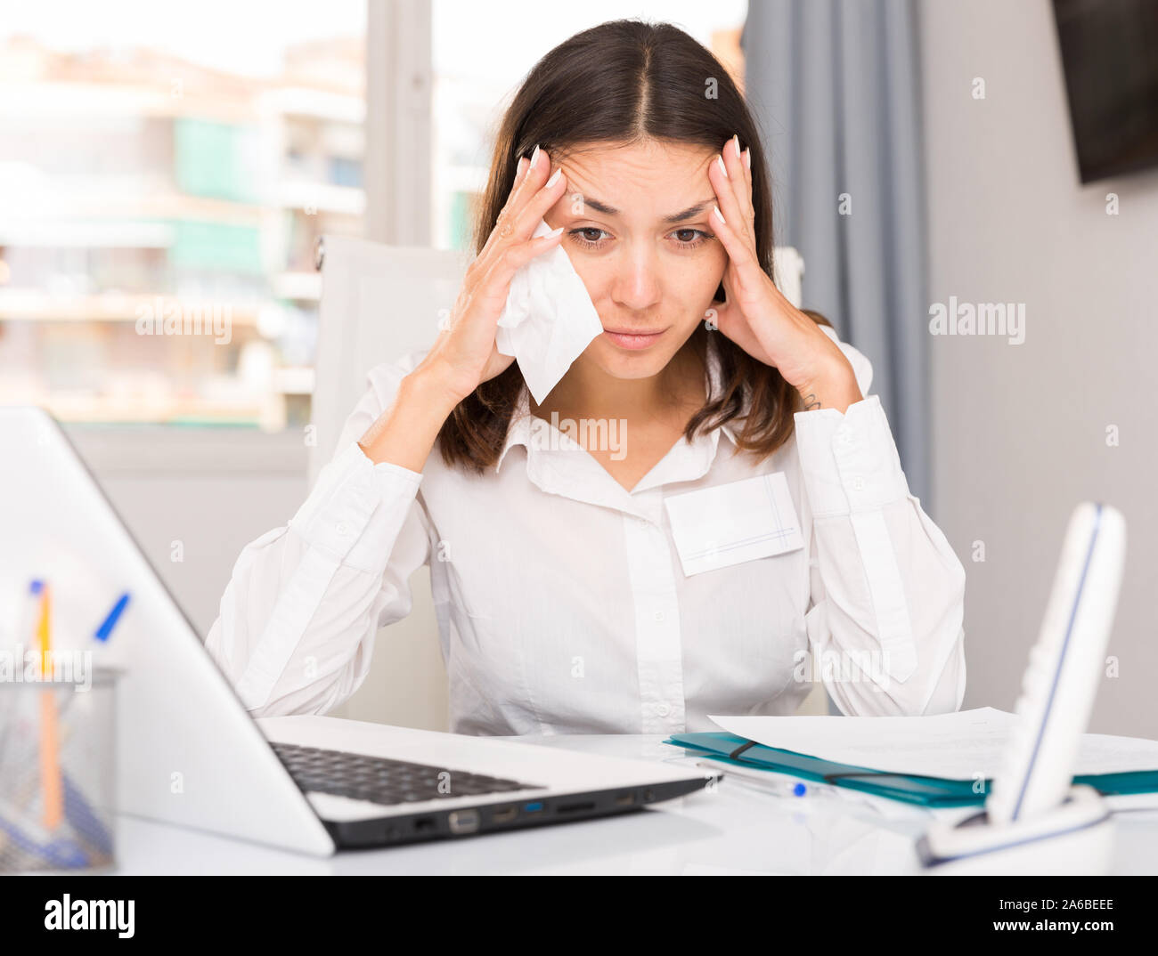 Upset woman crying and holding napkin at laptop at the office table ...