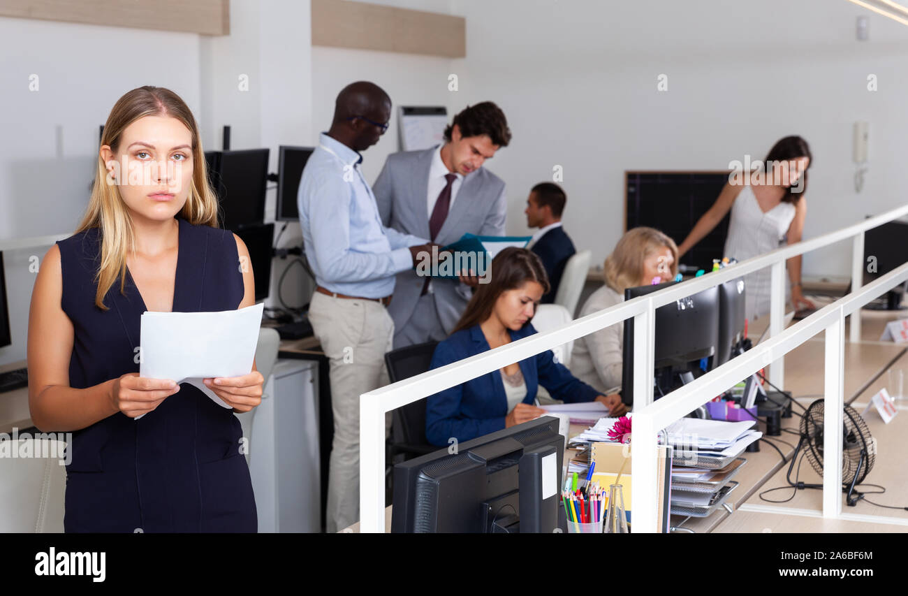 Puzzled and confused young woman standing with papers in hands in open ...