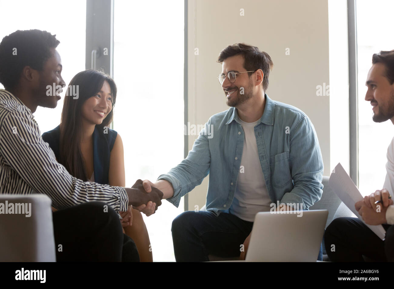 Smiling diverse business partners handshaking at group negotiations ...