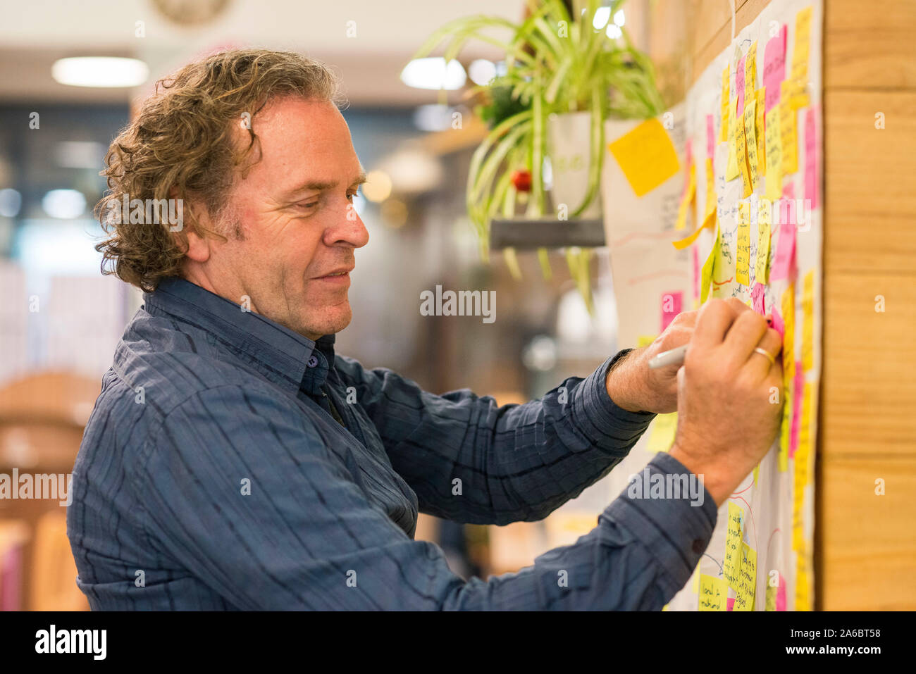 A man stands in a meeting and writes down ideas on post it notes on the ...