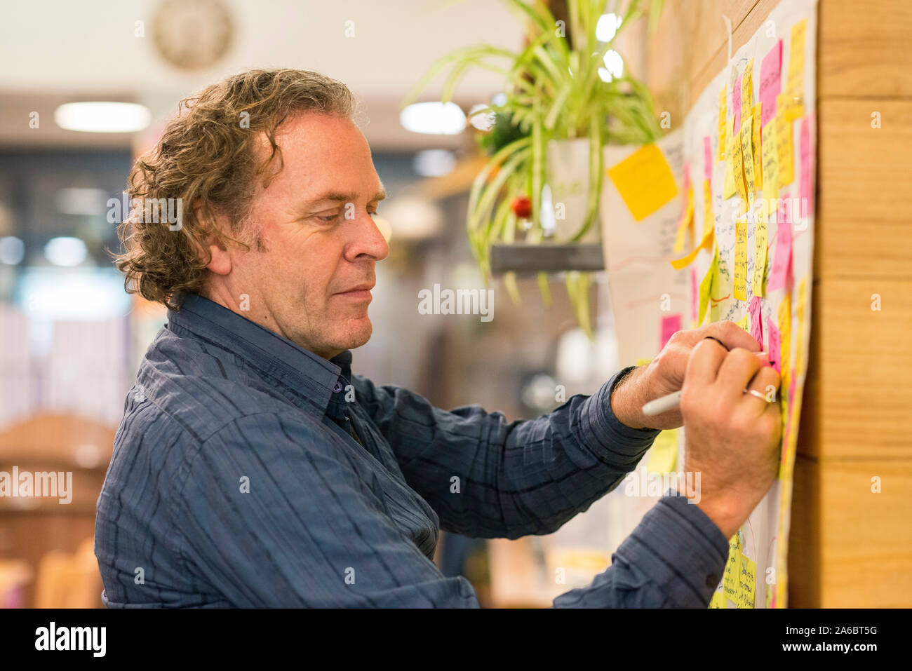 A man stands in a meeting and writes down ideas on post it notes on the ...
