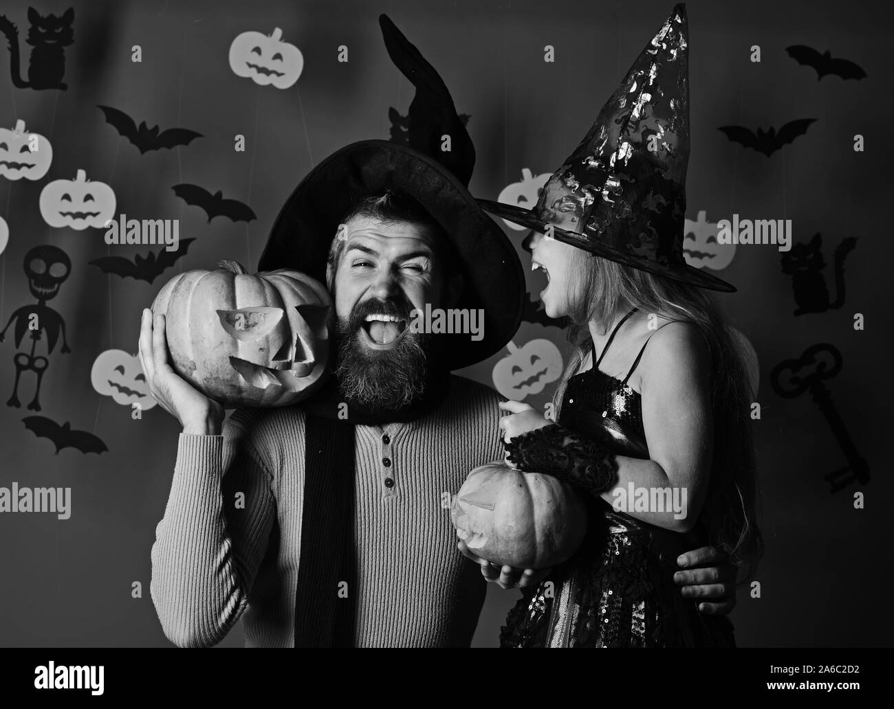 Wizard and little witch in black hats hold pumpkins. Father and ...