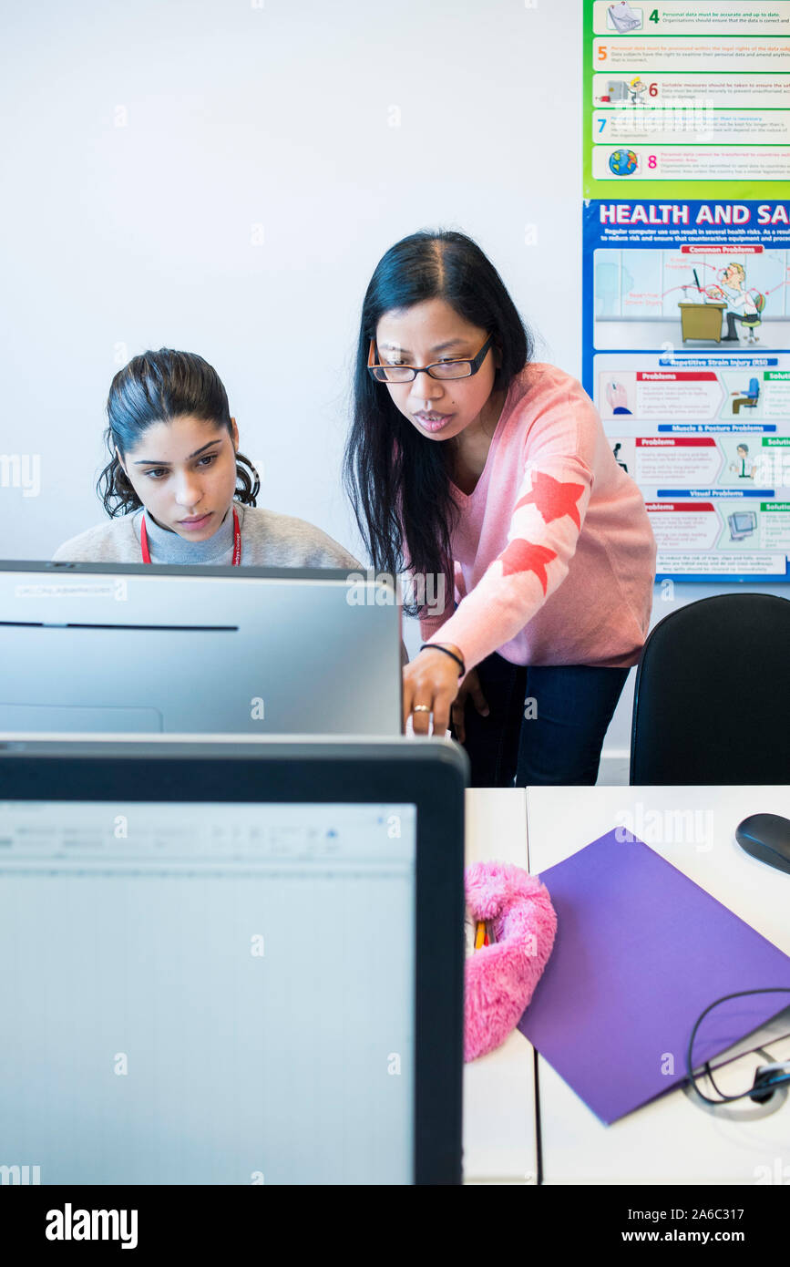 A computer technology class with students working and helping each ...