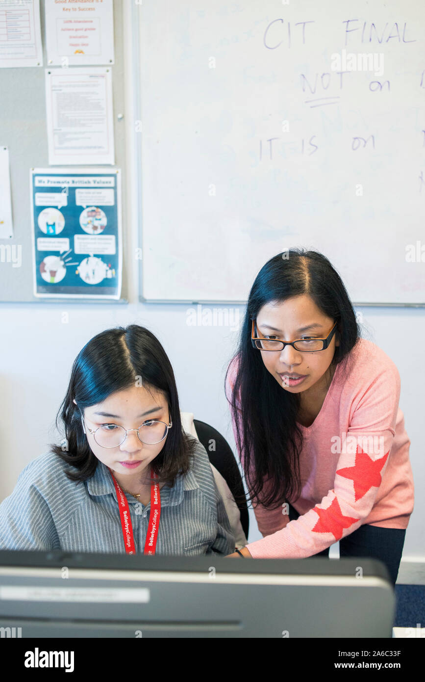 A computer technology class with students working and helping each ...