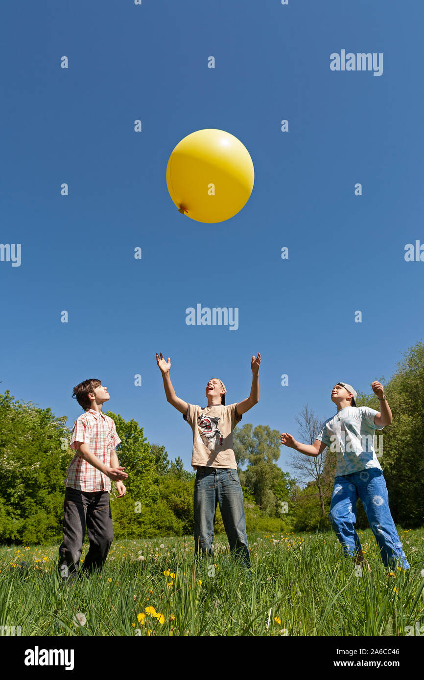 Three kids trying to catch a big yellow balloon Stock Photo - Alamy