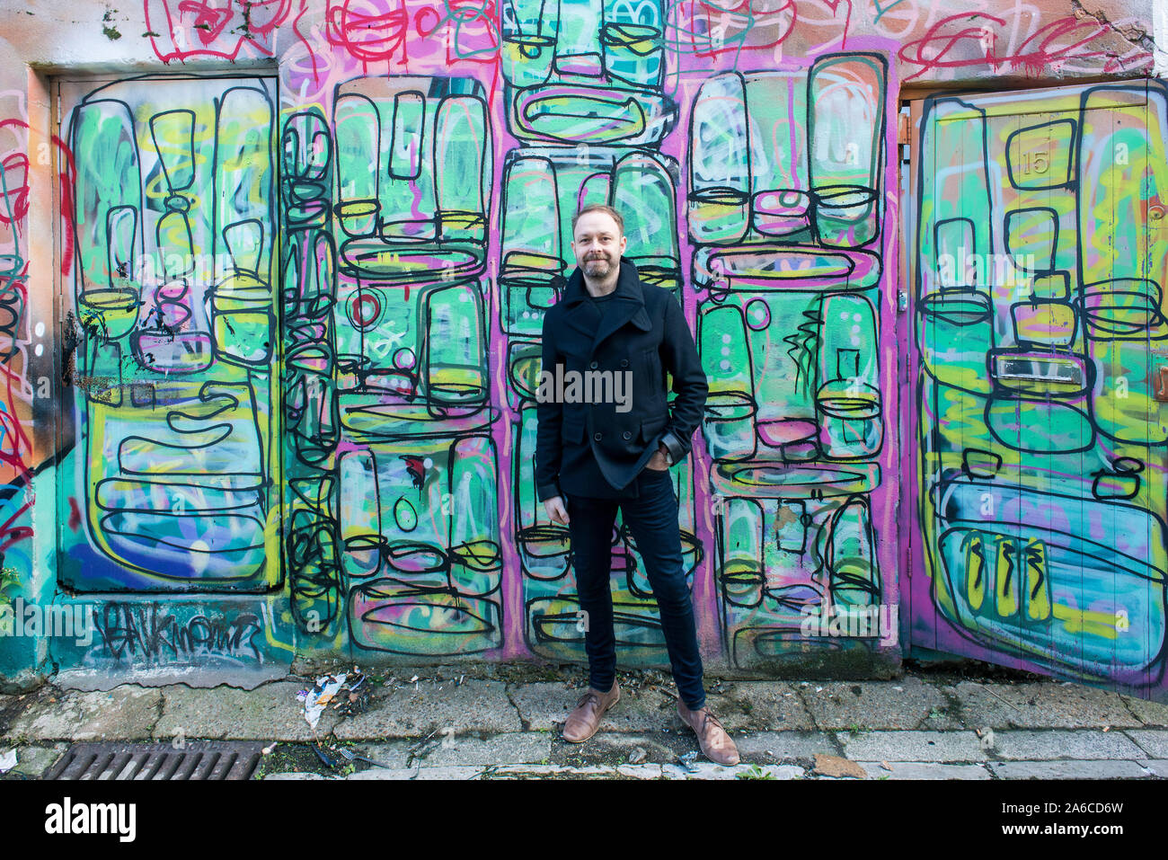 A man stands in front of a painted wall of graffiti Stock Photo - Alamy