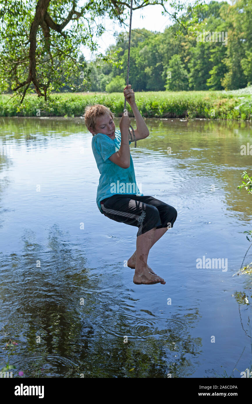 A boy is swinging on a rope above a river Stock Photo - Alamy