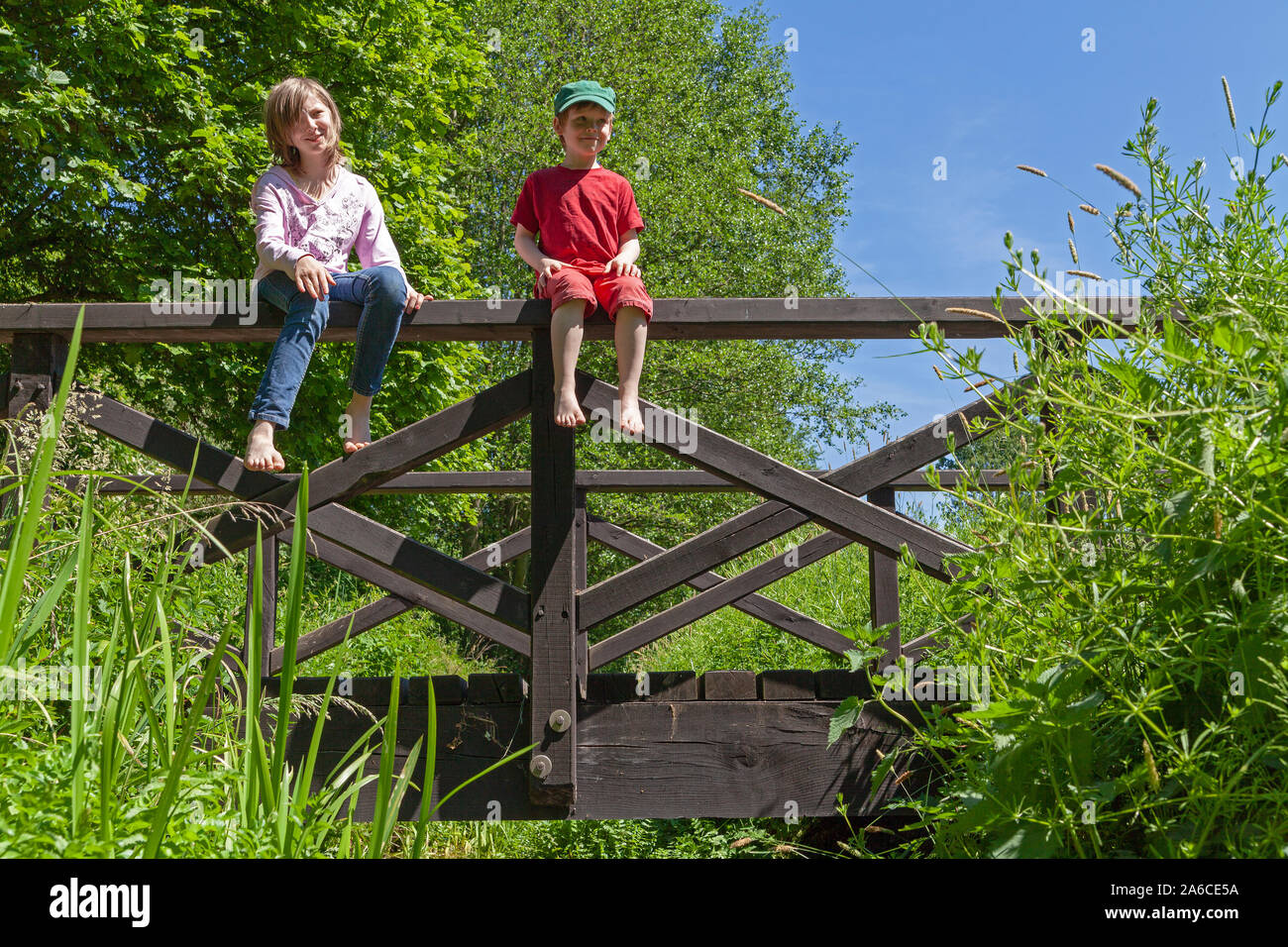 Two children are sitting on a railing of a wooden bridge Stock Photo ...