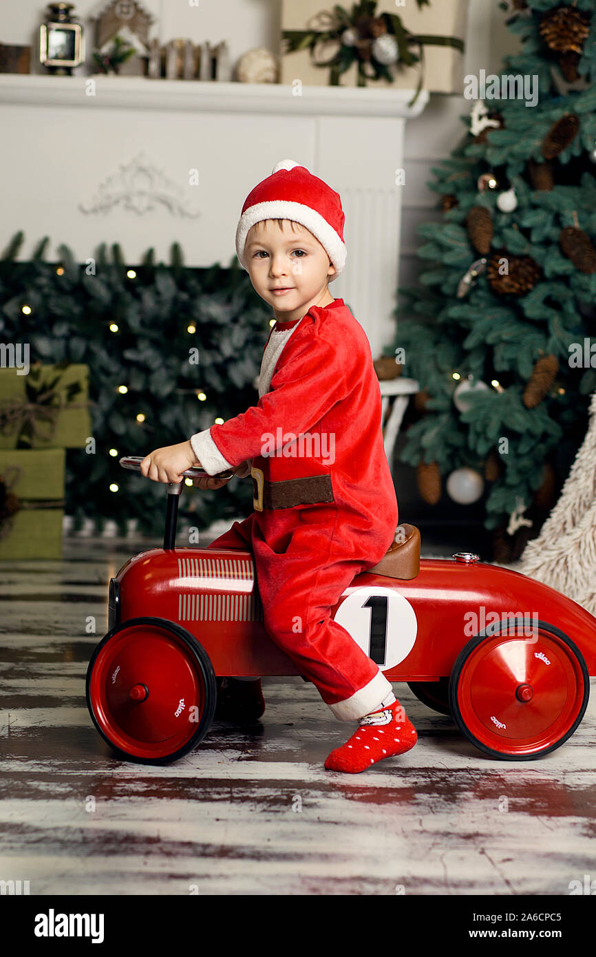 Little boy in santa claus costume rides a toy red car. Happy childhood ...
