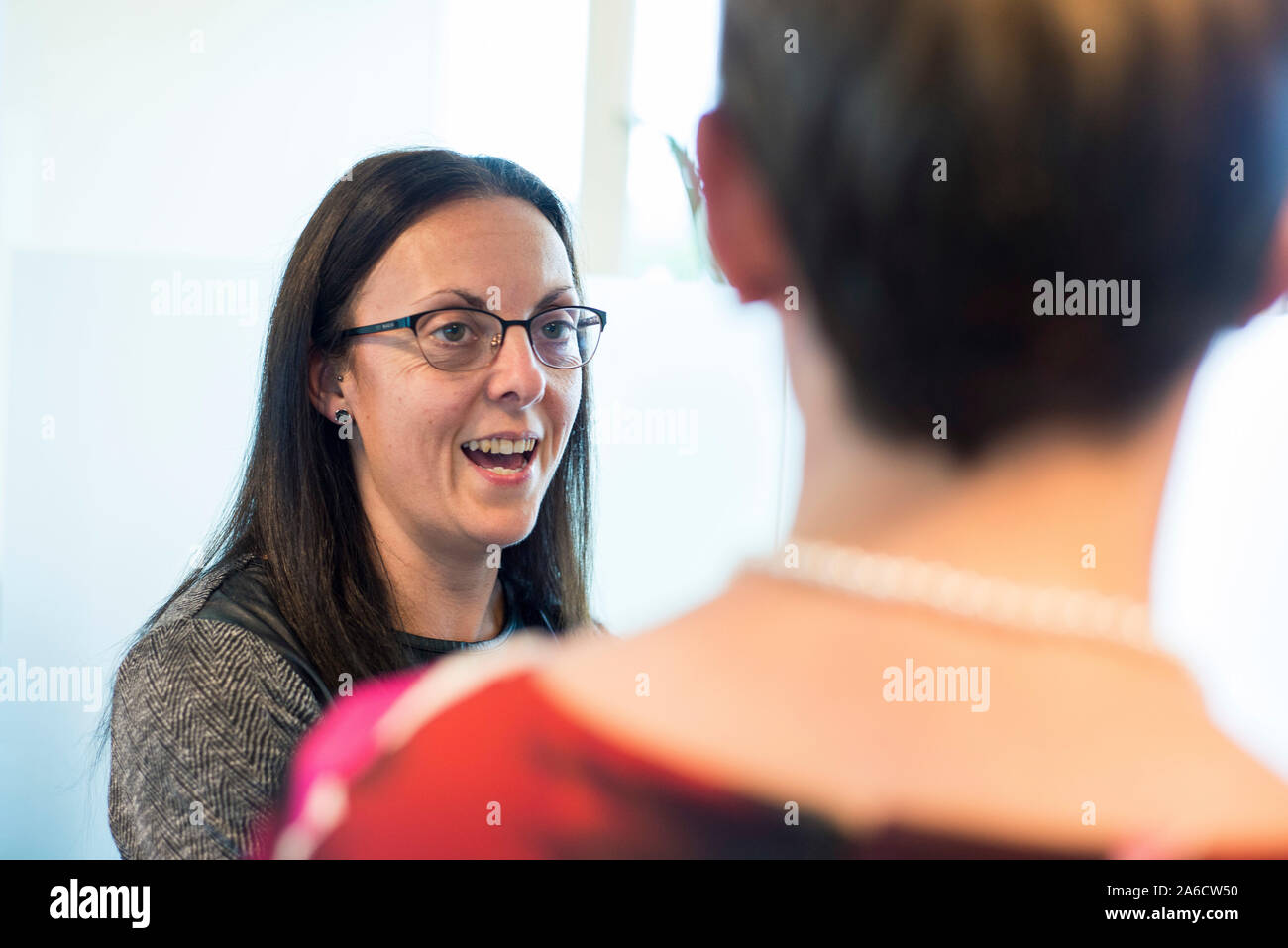 Two women stand in a corridor chatting at the office Stock Photo - Alamy