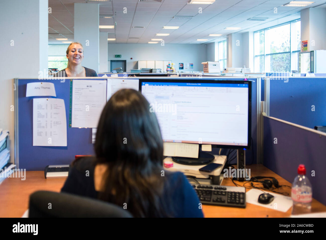 two female members of staff chat across an open plan office over the ...