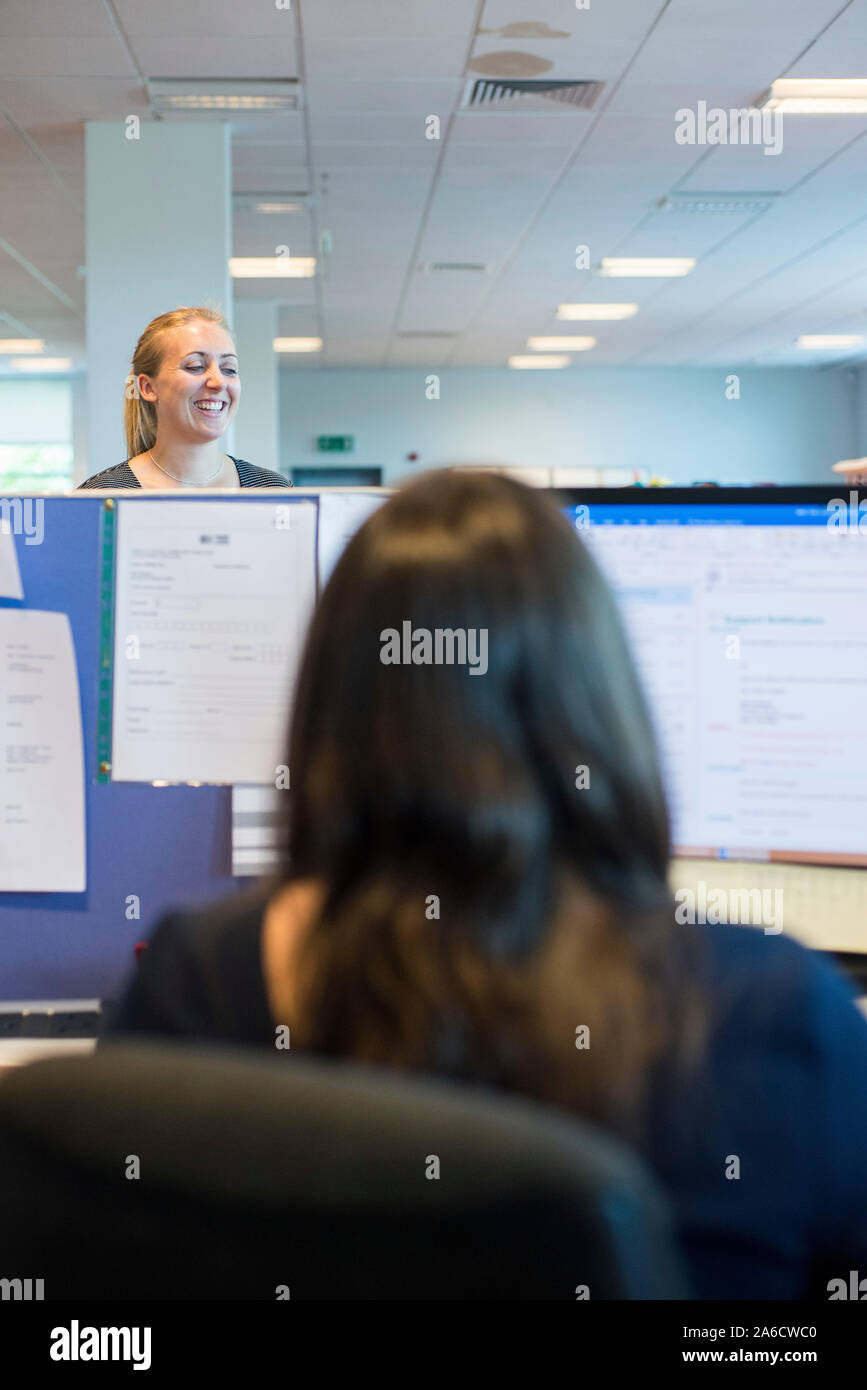 two female members of staff chat across an open plan office over the ...