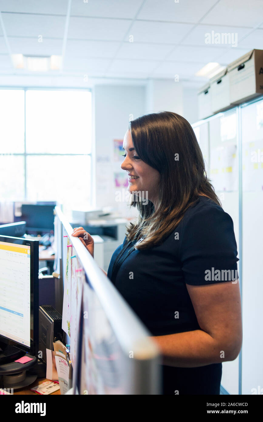 two female members of staff chat across an open plan office over the ...
