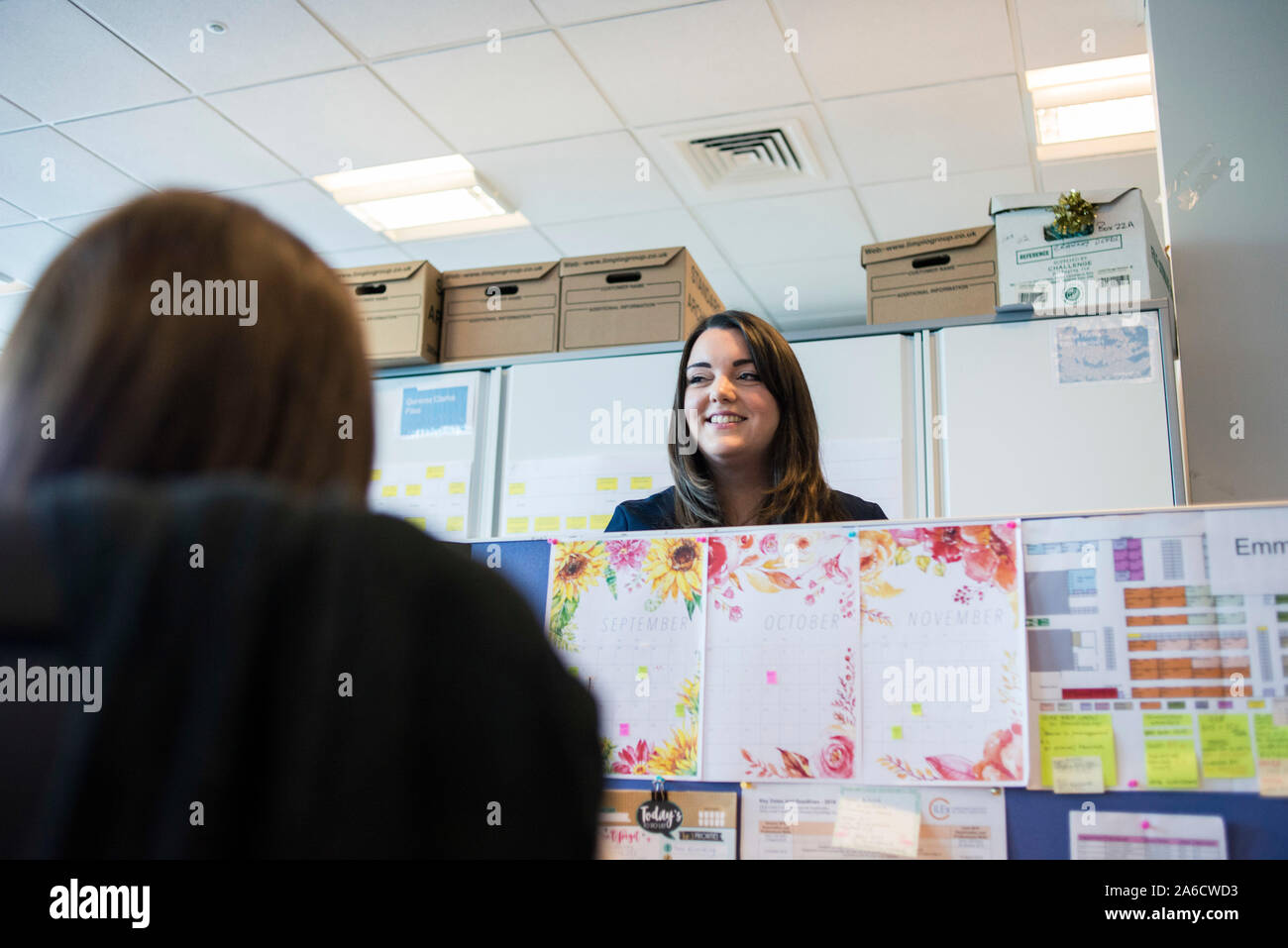 two female members of staff chat across an open plan office over the ...