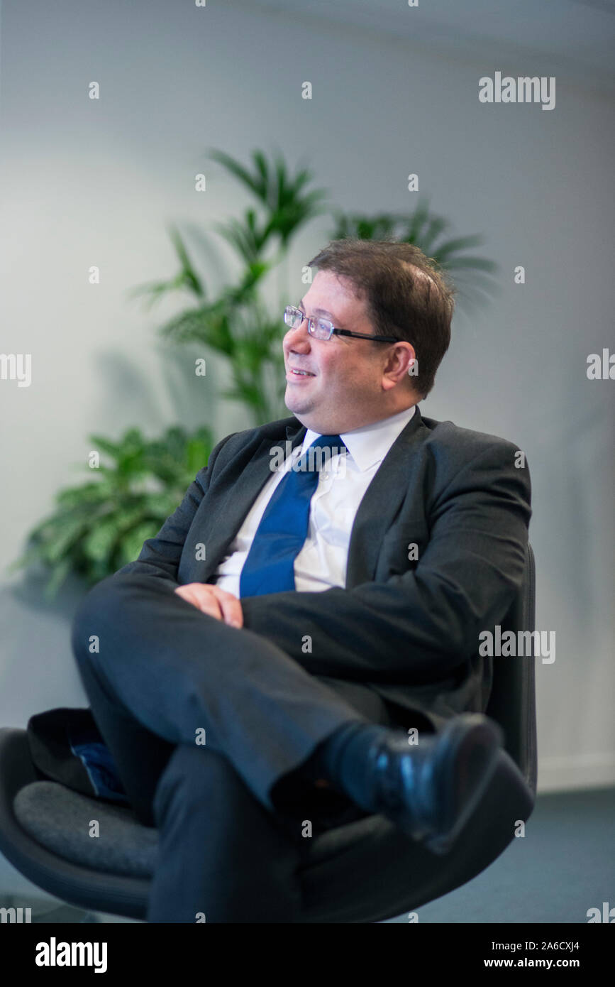A male office worker sits in an informal setting having a relaxed ...