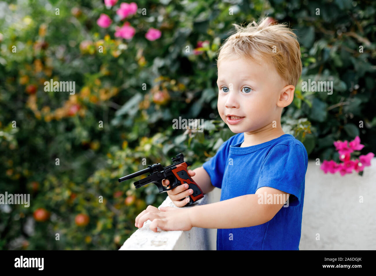 Cute kid boy with toy gun in green garden background Stock Photo - Alamy